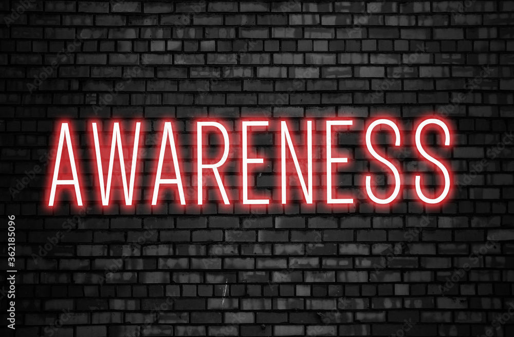 Awareness word glowing in pink neon color on dark black brick wall ...