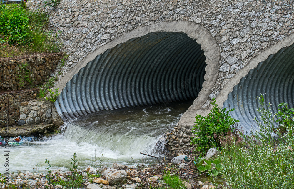 Water drains through pipes, under a bridge. Stock Photo | Adobe Stock