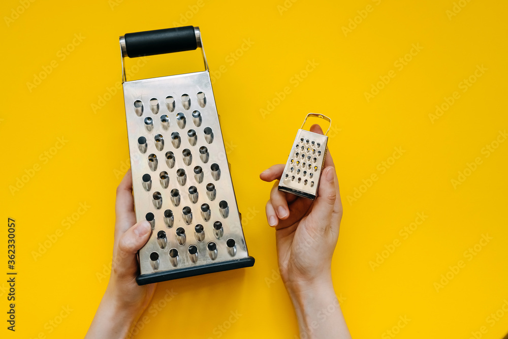 Human hands holding big and small sized graters on bright yellow ...