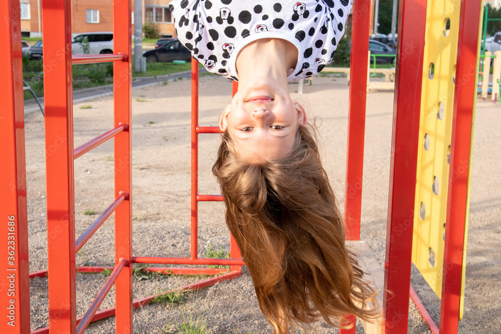 Happy girl child swinging upside down in the playground. Child plays on ...