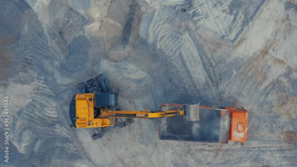 Aerial top down view of an excavator loading crushed stone into a dump ...
