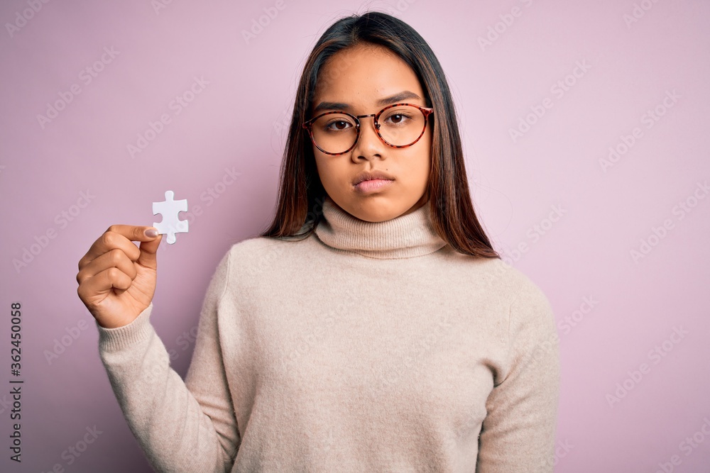 Young asian girl holding piece of puzzle standing over isolated pink ...