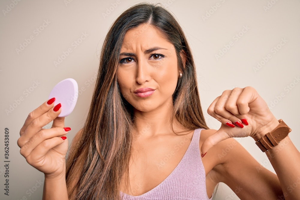 Young beautiful woman using beauty sponge with facial makeup over pink ...