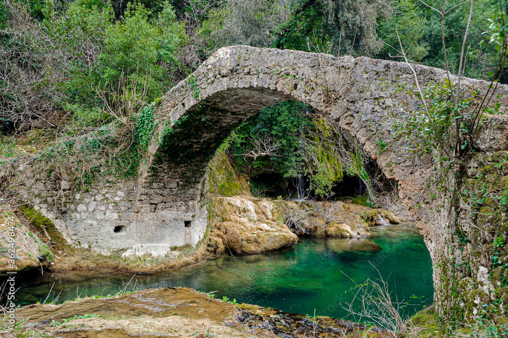 An old stone bridge over the river. An arch over a basin of green water ...