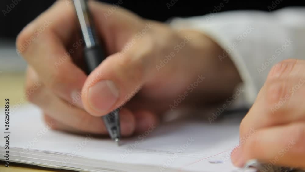 Low angle close up view of hand writing notes in notebook with pen ...