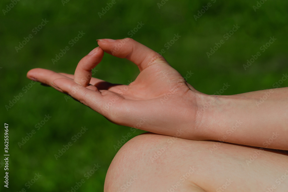 Woman meditating and sitting in lotus pose on the green grass, holding ...