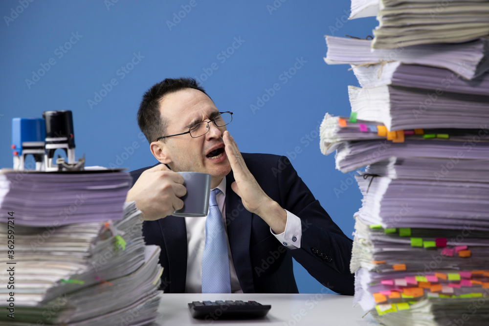tired office worker yawns tired sitting at desk with huge pile of ...
