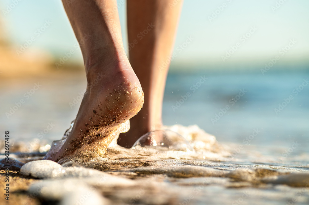 Close up of woman feet walking barefoot on sand beach in sea water ...