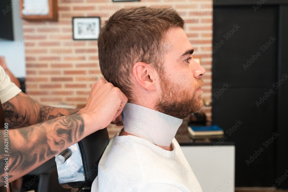 Hairdresser with tattoos putting a neck strip around the customer's ...