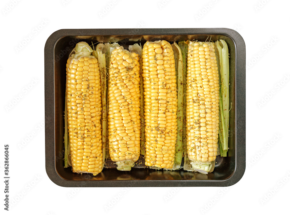 Isolated black baking tray with corn cobs with spiced, leaves on a ...
