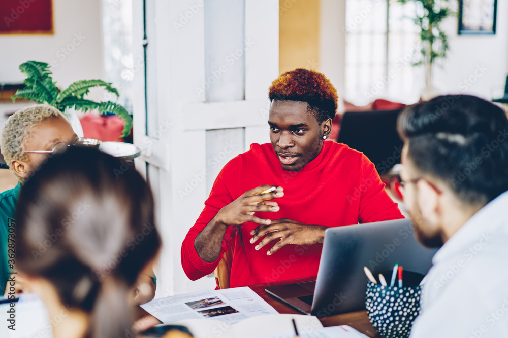 Dark skinned male team member gesturing while explaining information to ...