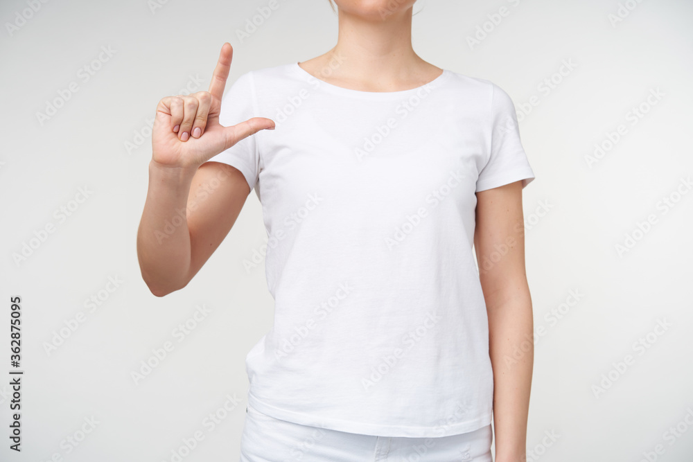 Indoor shot of young female raising her hand while forming letter l ...