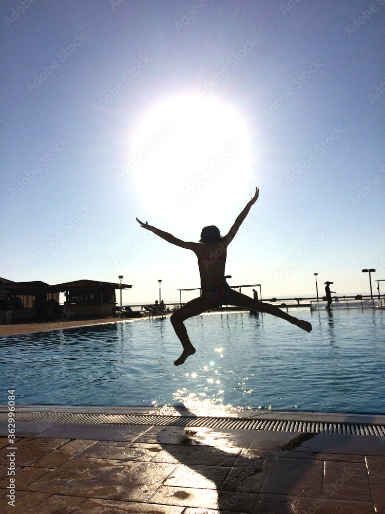 silhouette of a child jumping in a swimming pool with open arms and ...