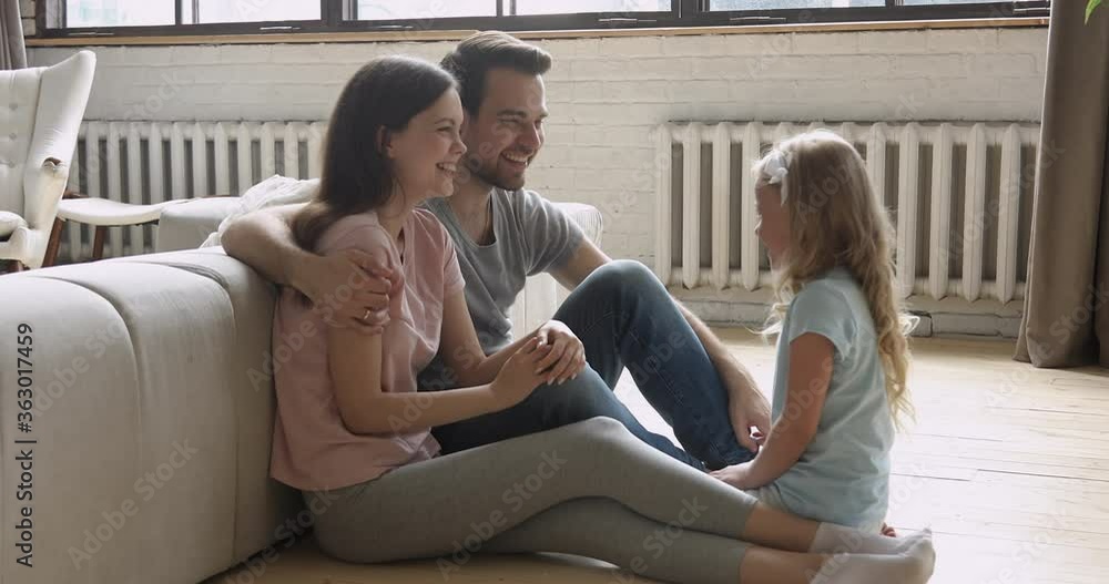 Happy family mom dad and little cute child daughter talking laughing embracing sit on floor ...