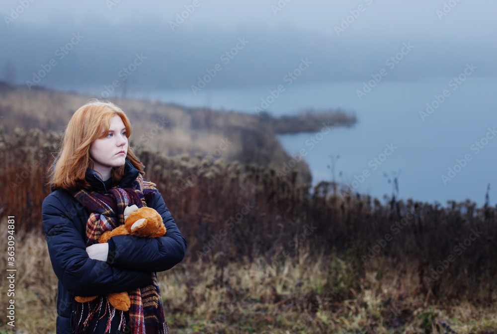 Sad blonde teenager girl hugging teddy bear by foggy lake. Concept of ...