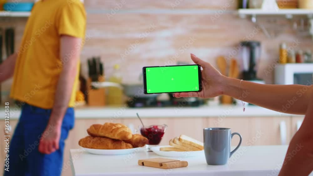 Girlfriend showing smartphone with green screen in kitchen and husband ...
