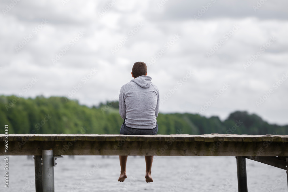 One young adult man sitting alone on edge of footbridge and staring at ...