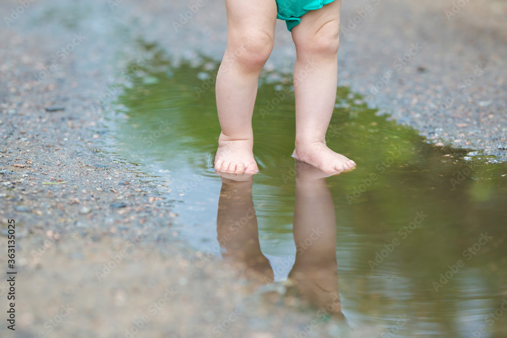 Baby legs standing in shallow puddle after warm rain. Front view ...
