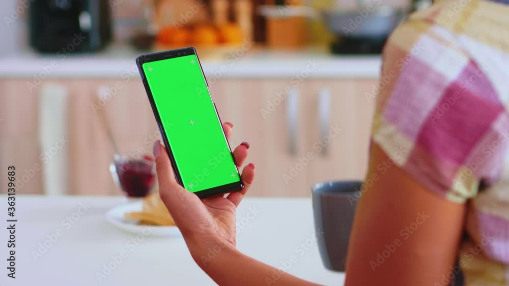 Woman looking at phone with green touchscreen while drinking a cup of ...