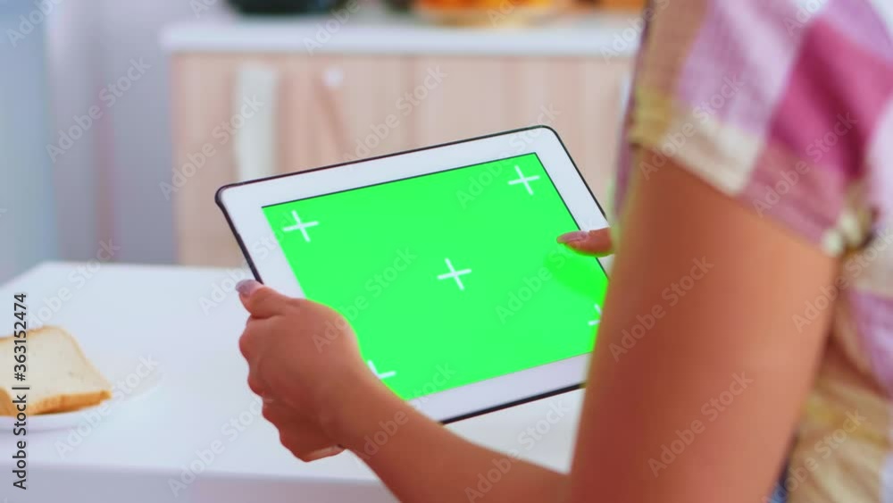 Woman browsing on tablet computer with green screen in kitchen. Green ...