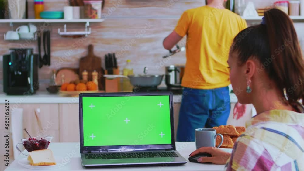 Woman entrepreneur working on laptop with green screen in kitchen while ...