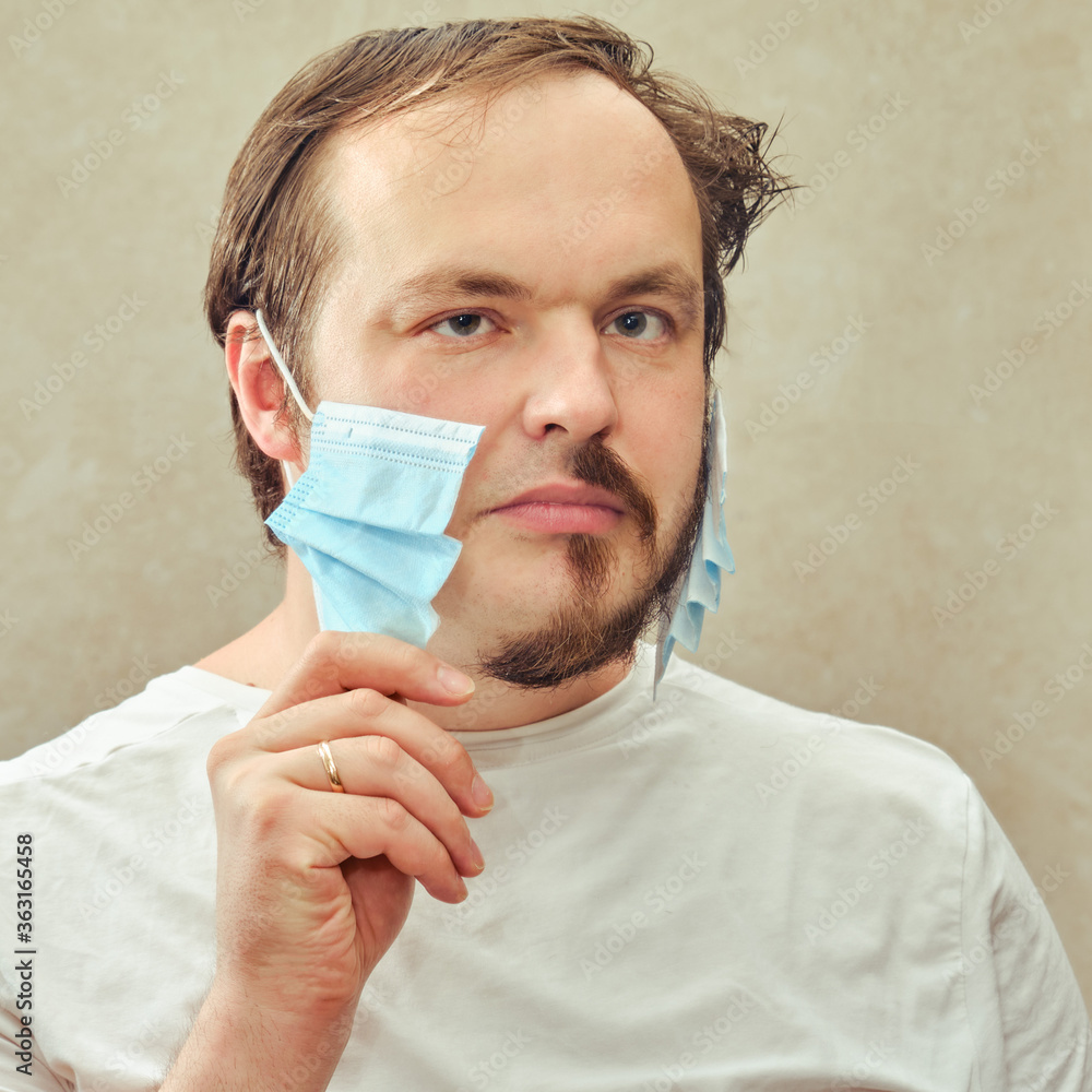 An adult man with half a beard removes the medical mask from his face ...