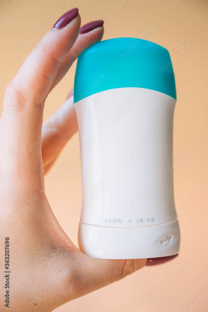 Female hand holding dry deodorant in a white bottle on a bright ...