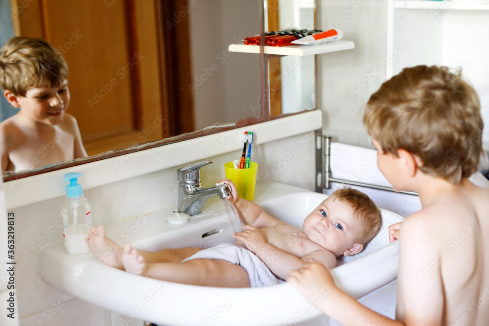 Cute adorable baby taking bath in washing sink and grab water tap. Kid ...