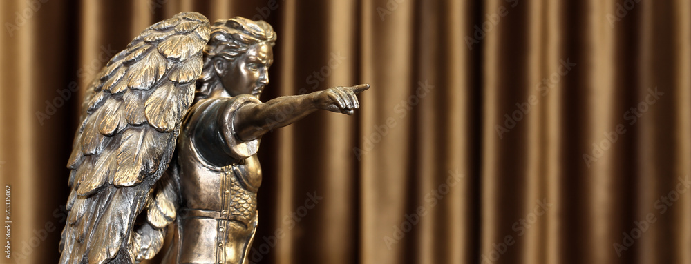 A bronze statuette of the Archangel Michael points a finger forward ...