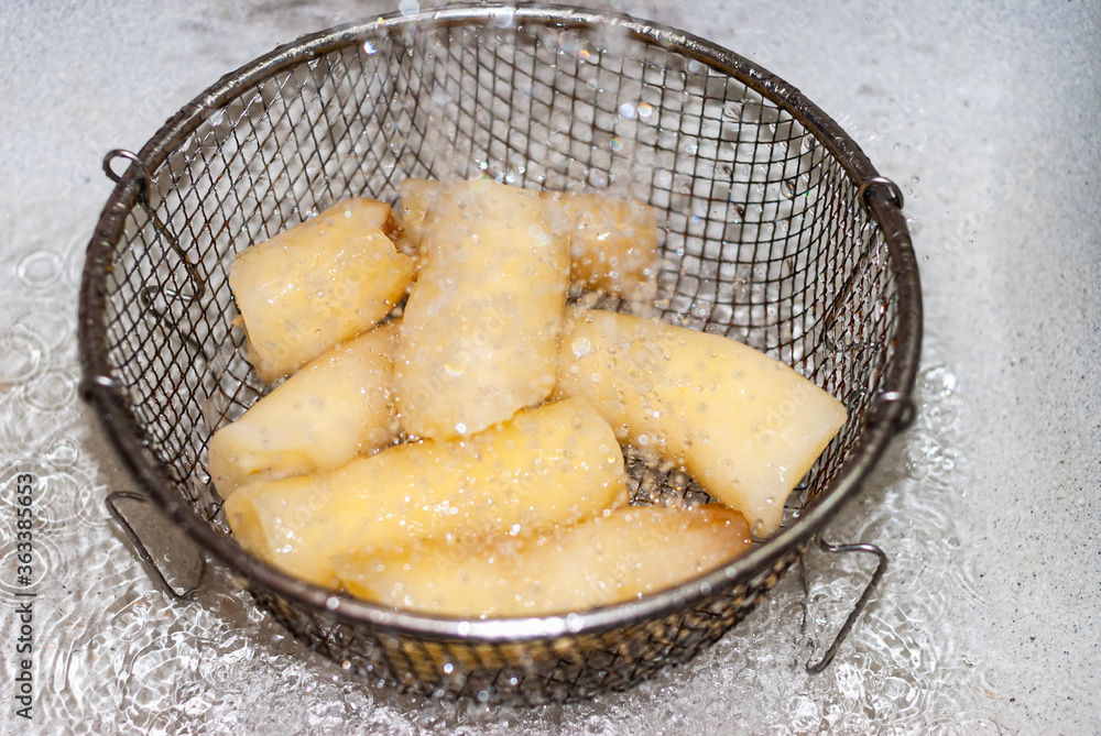 washing cassava with water in a metal strainer, Manihot esculenta ...