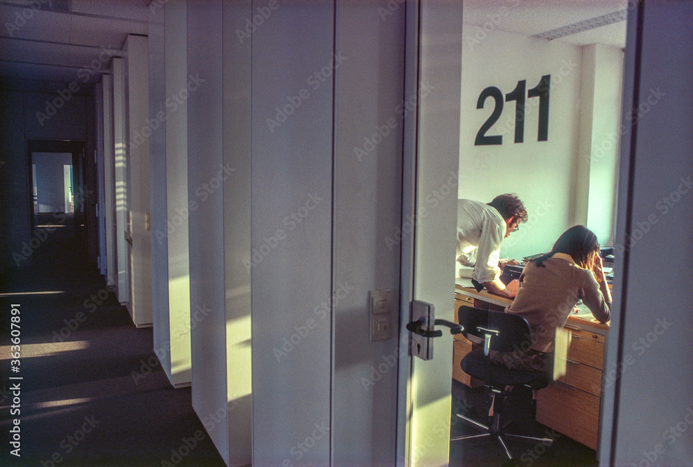 Two people hunched over desk in as seen through office doorway. Stock ...