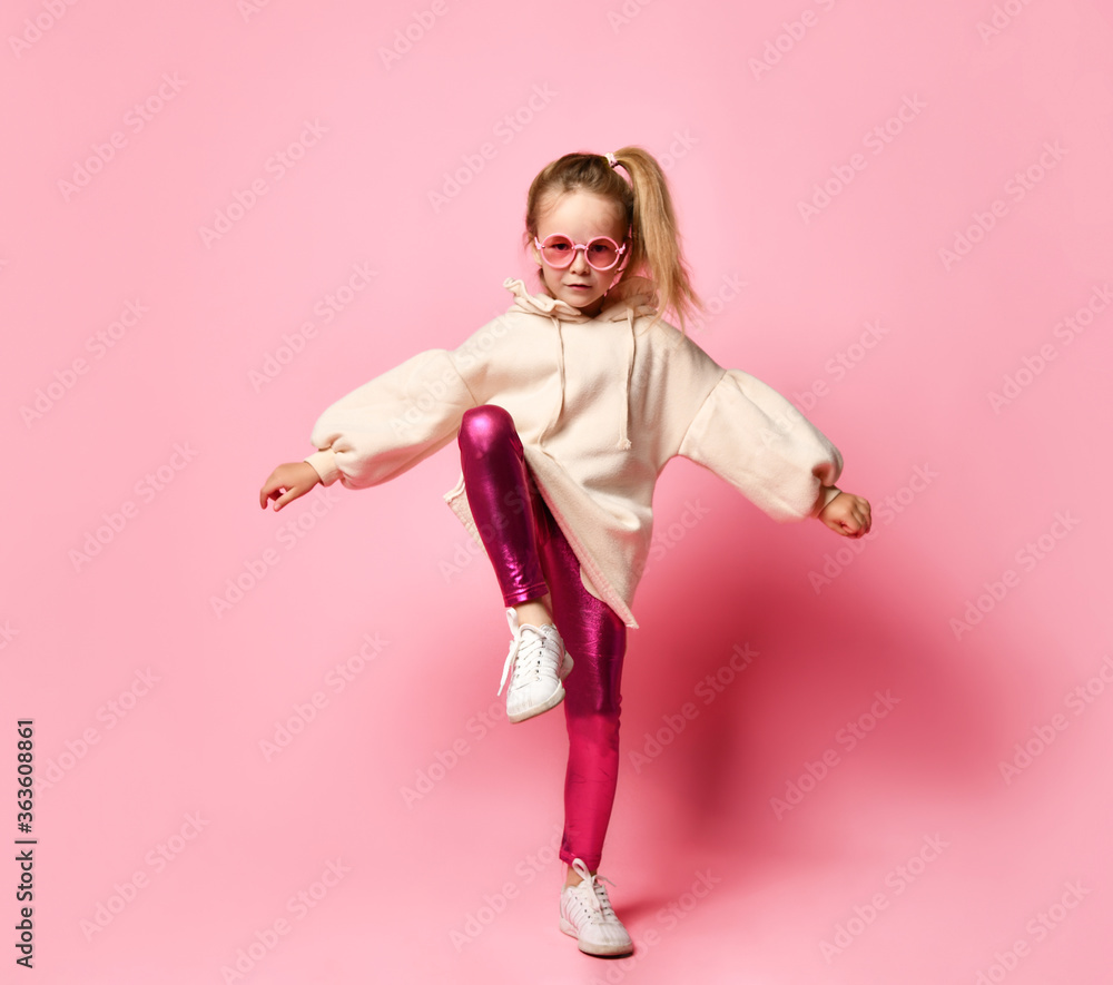 Concentrated little girl posing on one leg raising up her knee and ...