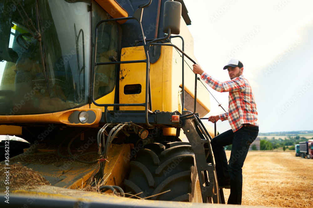 Harvester machine driver climbing into a cab to harvest his wheat field ...