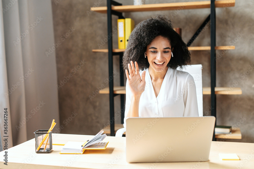 Cheerful biracial young woman uses laptop for video call. A glad girl ...