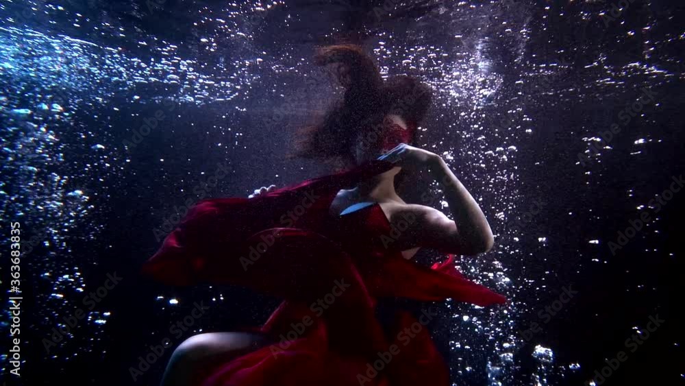 Close-up of a girl who is under water, she is wearing a long red dress ...