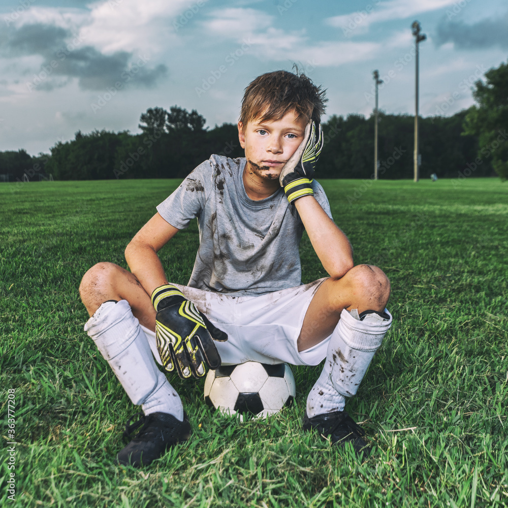 Muddy and tired young soccer boy sitting on ball after a game Stock ...