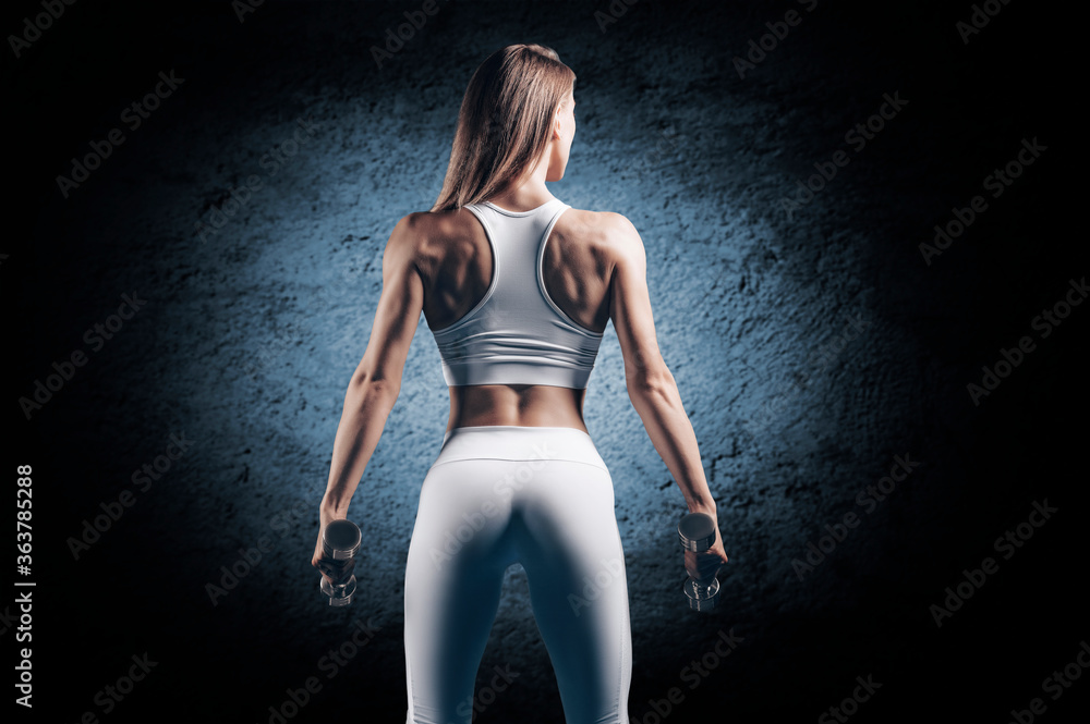 Adorable girl posing in the gym with dumbbells. Back view. The concept ...