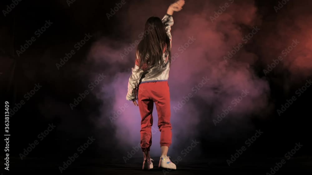 A sports young girl with long hair dances hip-hop with her back to the ...