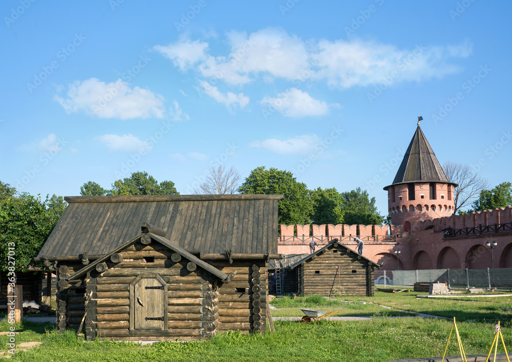 Building a wooden rustic log houses next to the fortress brick wall ...