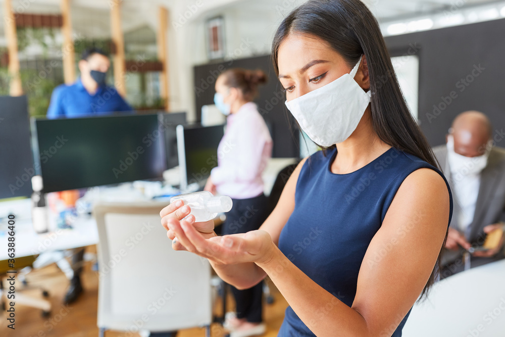 Woman using face mask in office while disinfecting hands Stock Photo ...