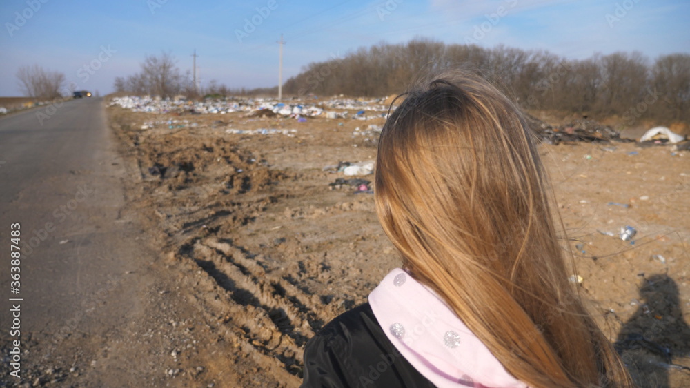 Little girl goes on the road against the background of garbage dump ...