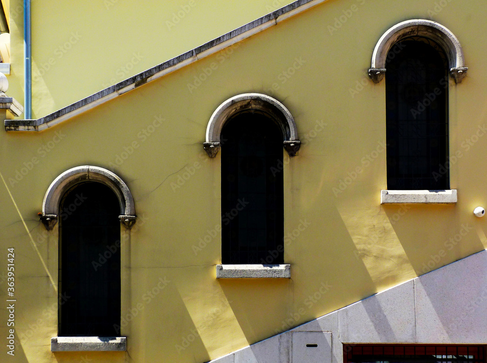 Three arched windows in yellow stucco exterior wall stepping up along ...