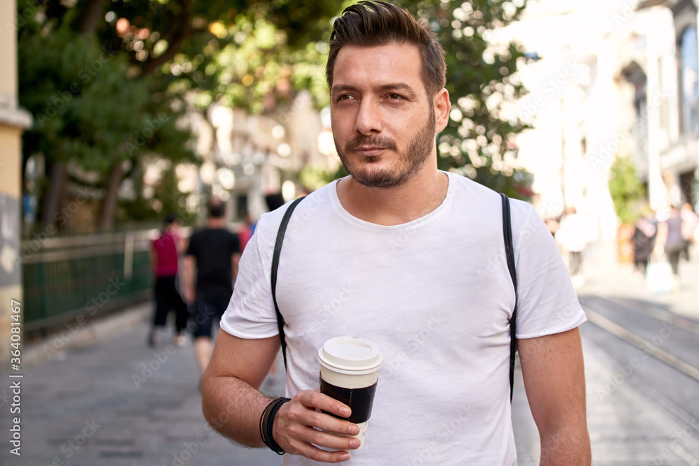 The man walking in the crowded street with his coffee in his hand is ...
