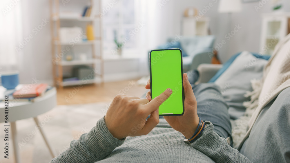 Man at Home Lying on a Couch using Smartphone with Green Mock-up Screen ...