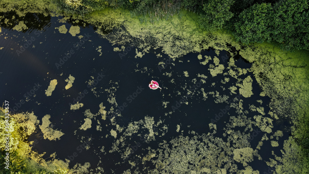 Girl in a swamp on an inflatable bright circle. Around visible tina and ...