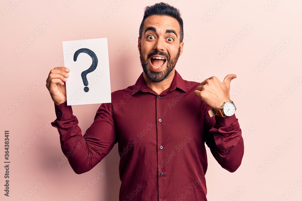 Young hispanic man holding question mark pointing thumb up to the side ...