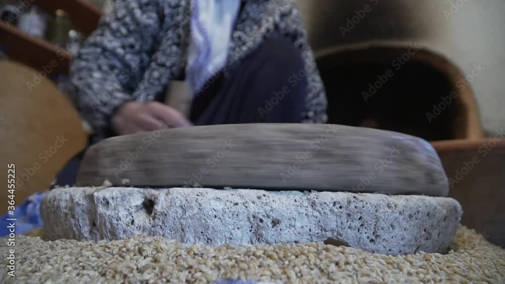 The ancient quern stone hand mill with grain. The woman grinds the ...