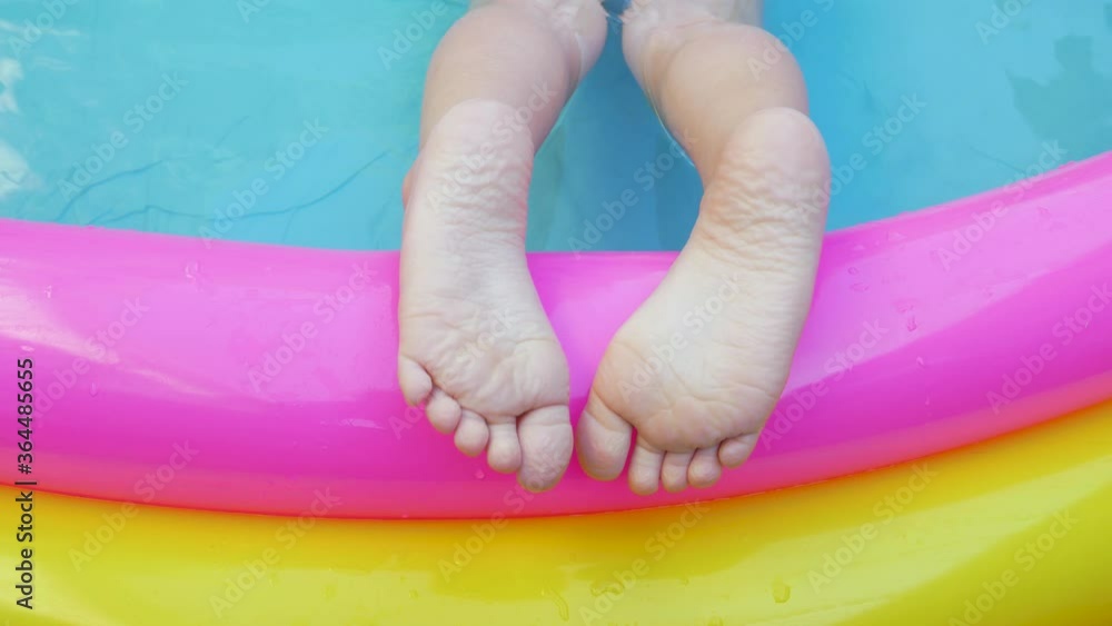 Kids feet laying on colorful rainbow inflatable swimming pool. Young ...