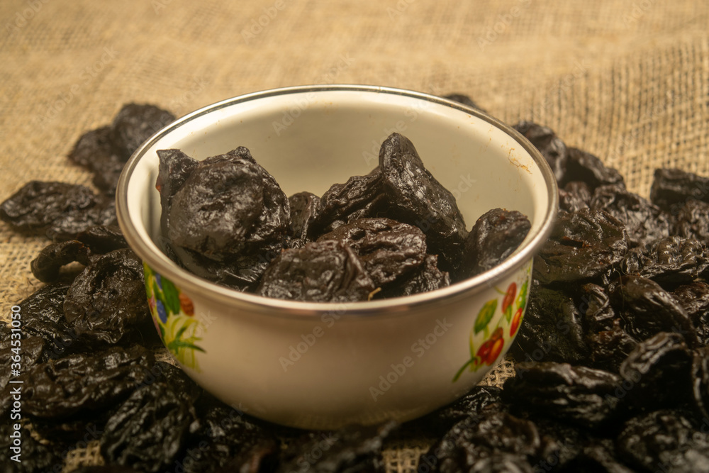 Dried prunes in a metal bowl and dried prunes scattered on a background ...
