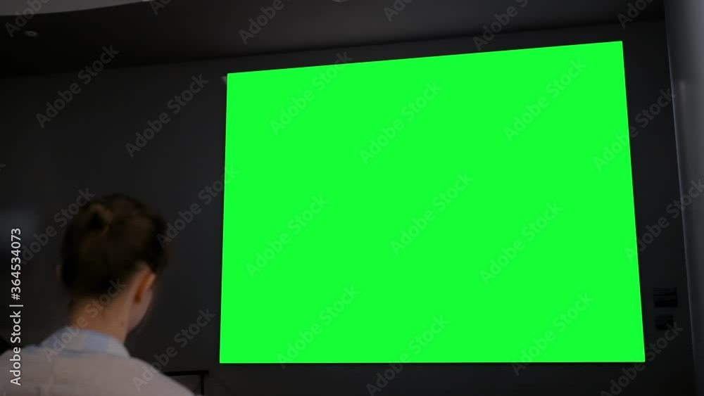 Woman looking at large wall blank interactive green display in dark ...
